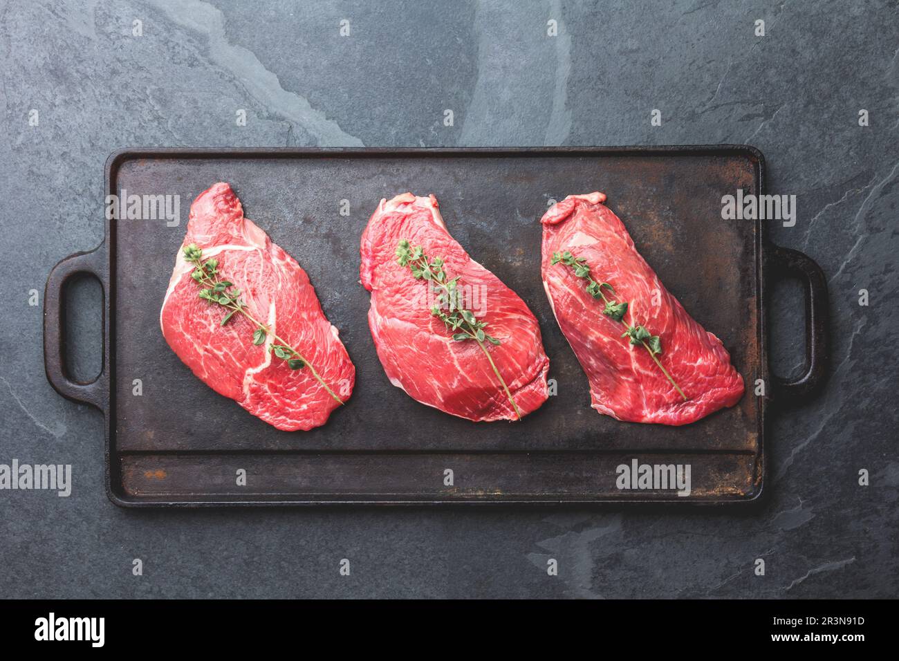 Raw beef steaks with herbs and spices on cast iron frying board, top ...