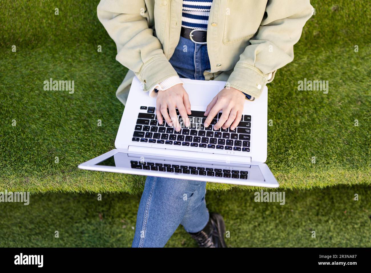 From above unrecognizable young remote worker sitting on a grassy knoll ...