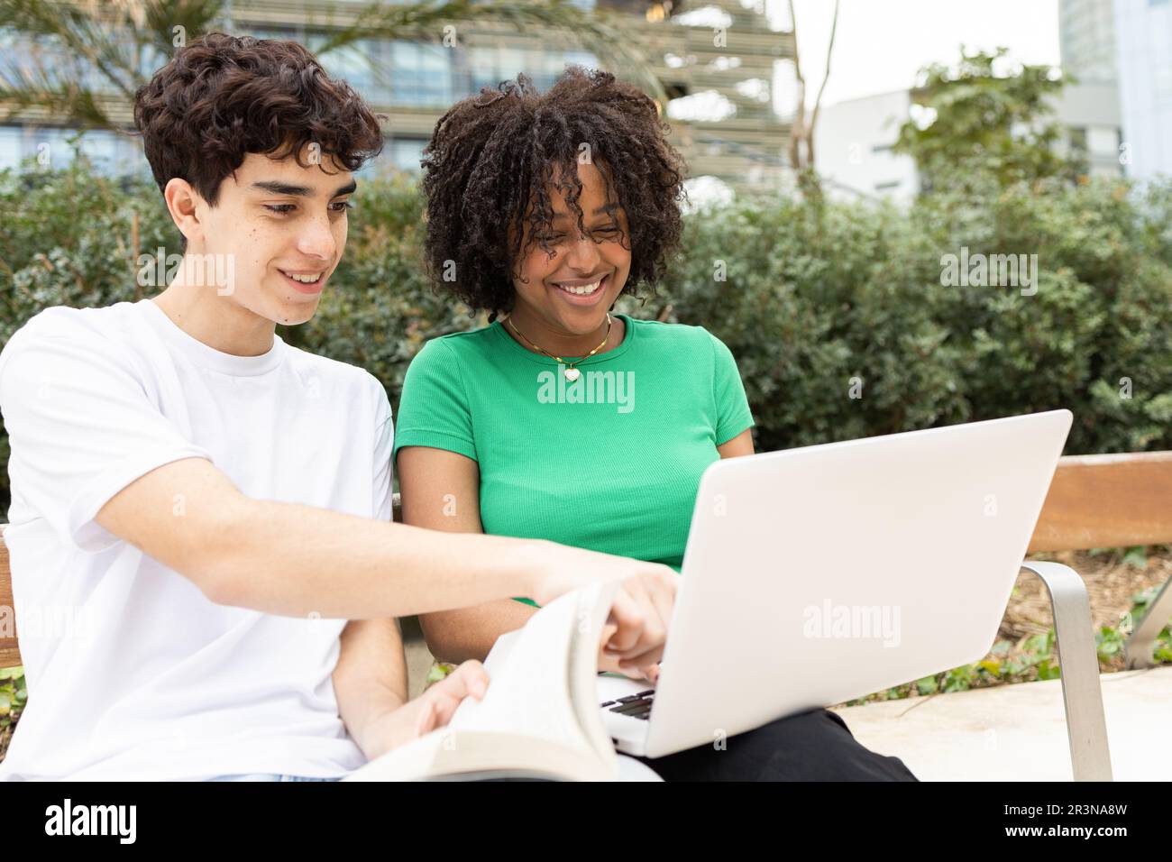 Cheerful young students sitting together on cement border with legs ...