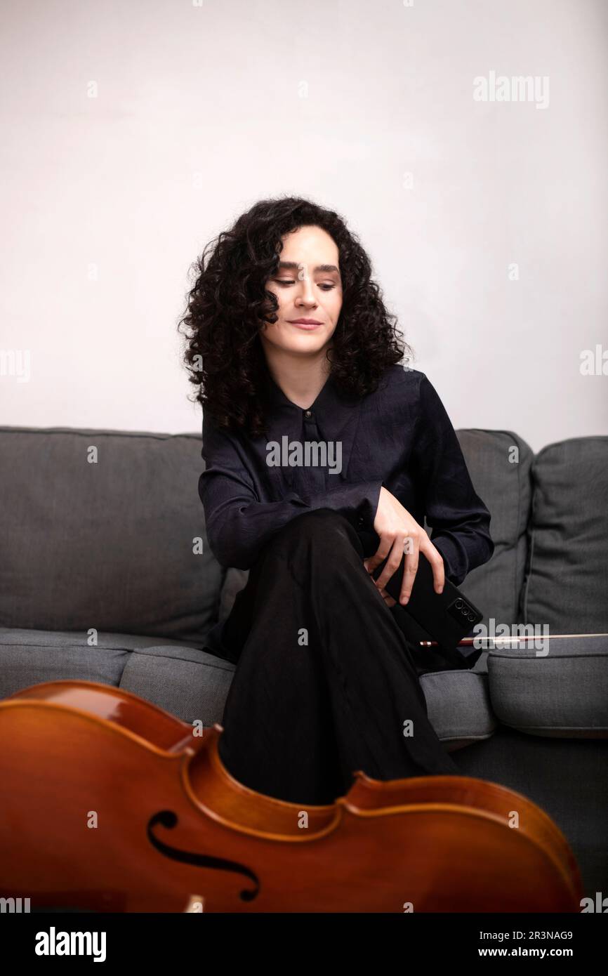 Positive female musician in black clothes sitting on cozy sofa with ...