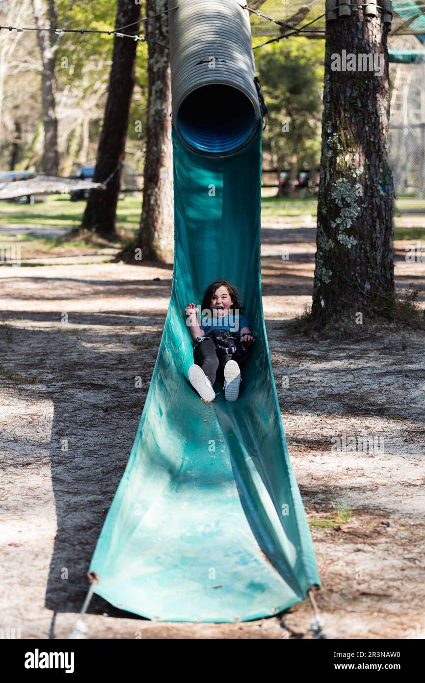 Happy preteen girl with tongue out sliding down in sunny park with tall ...