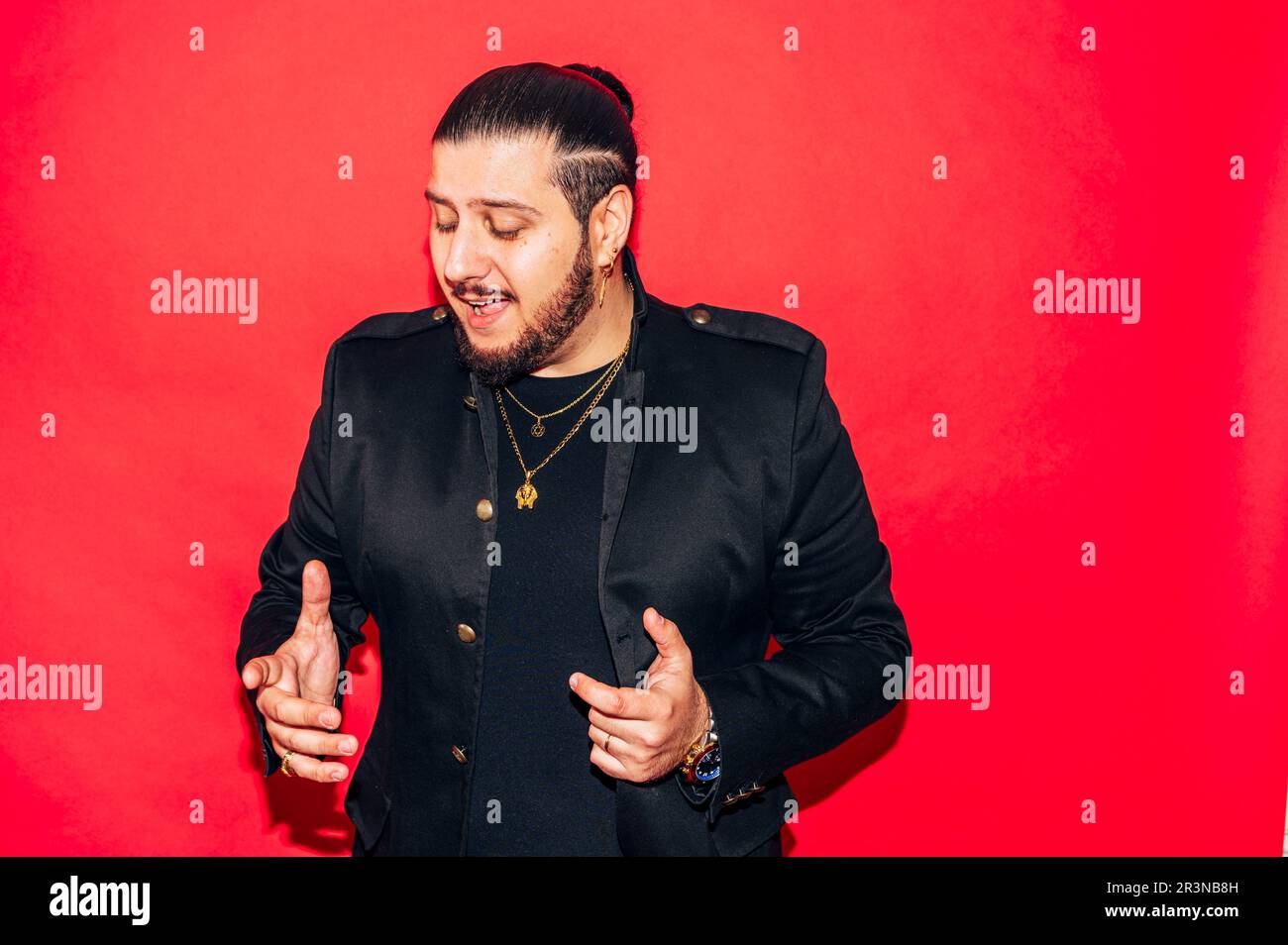 Calm bearded young male singer in black suit with accessories pointing ...