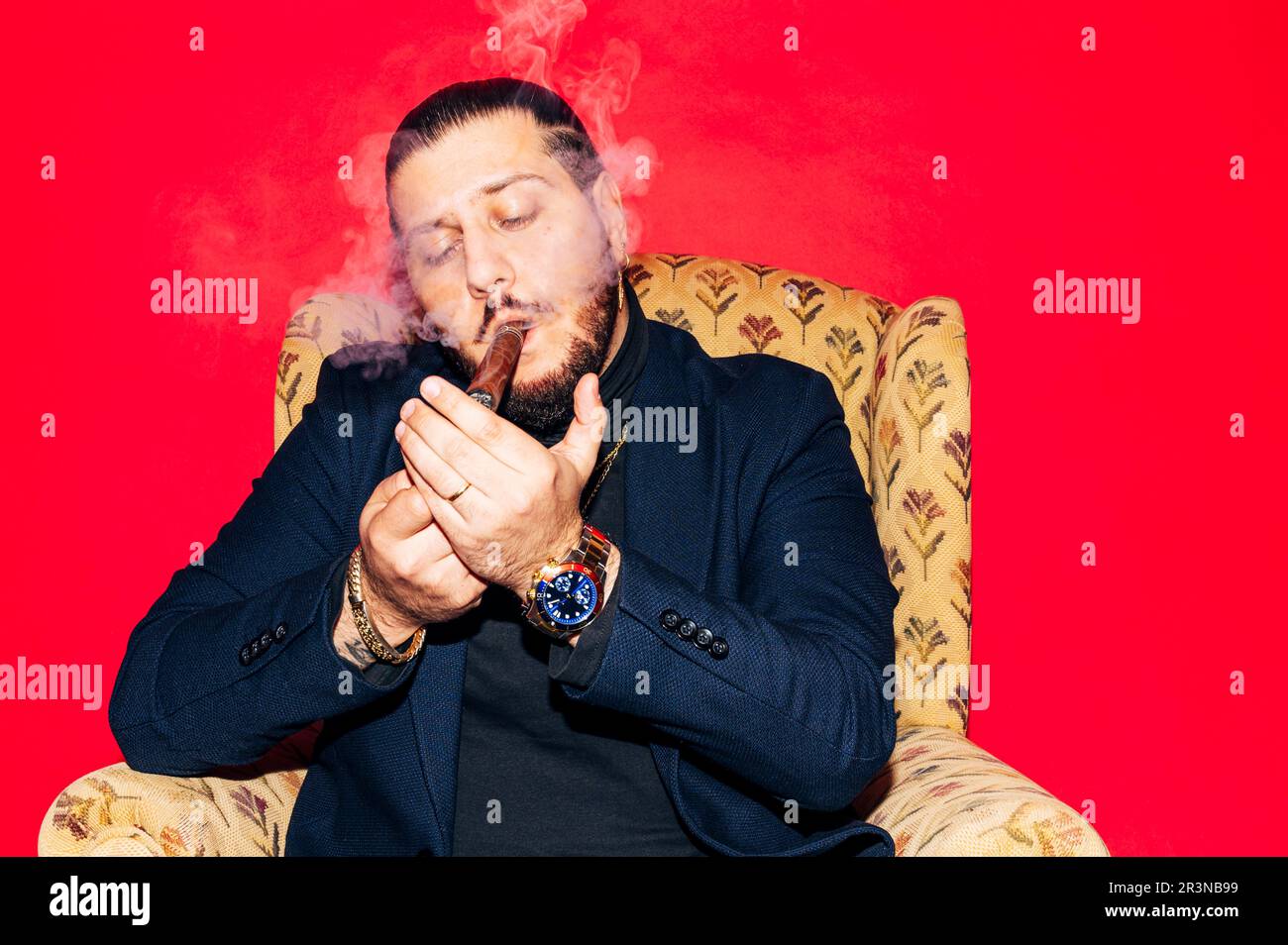 Serious bearded male model in suit smoking cigar while sitting in ...