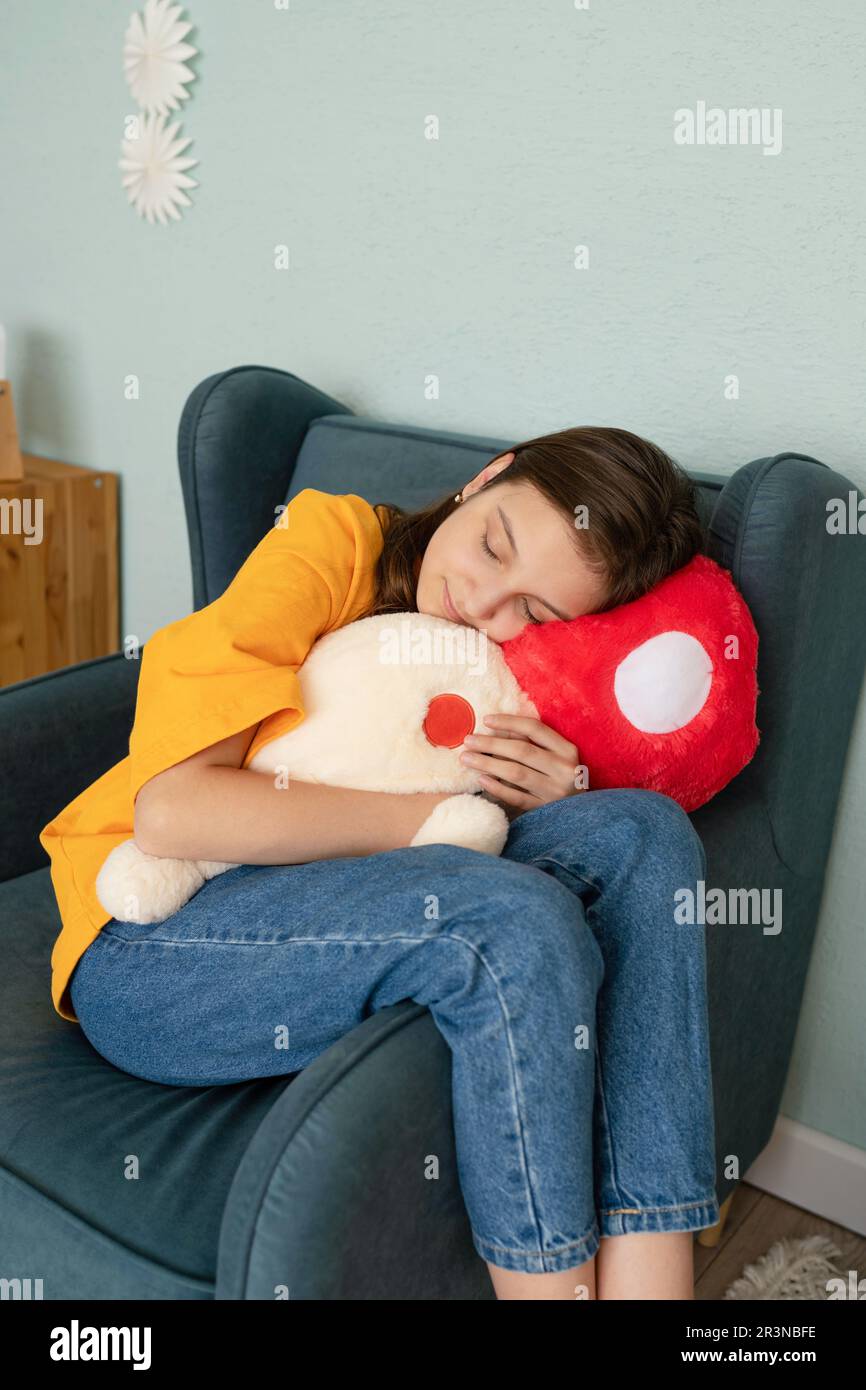 Adorable teenage girl cuddling favorite plush pillow while smiling and ...