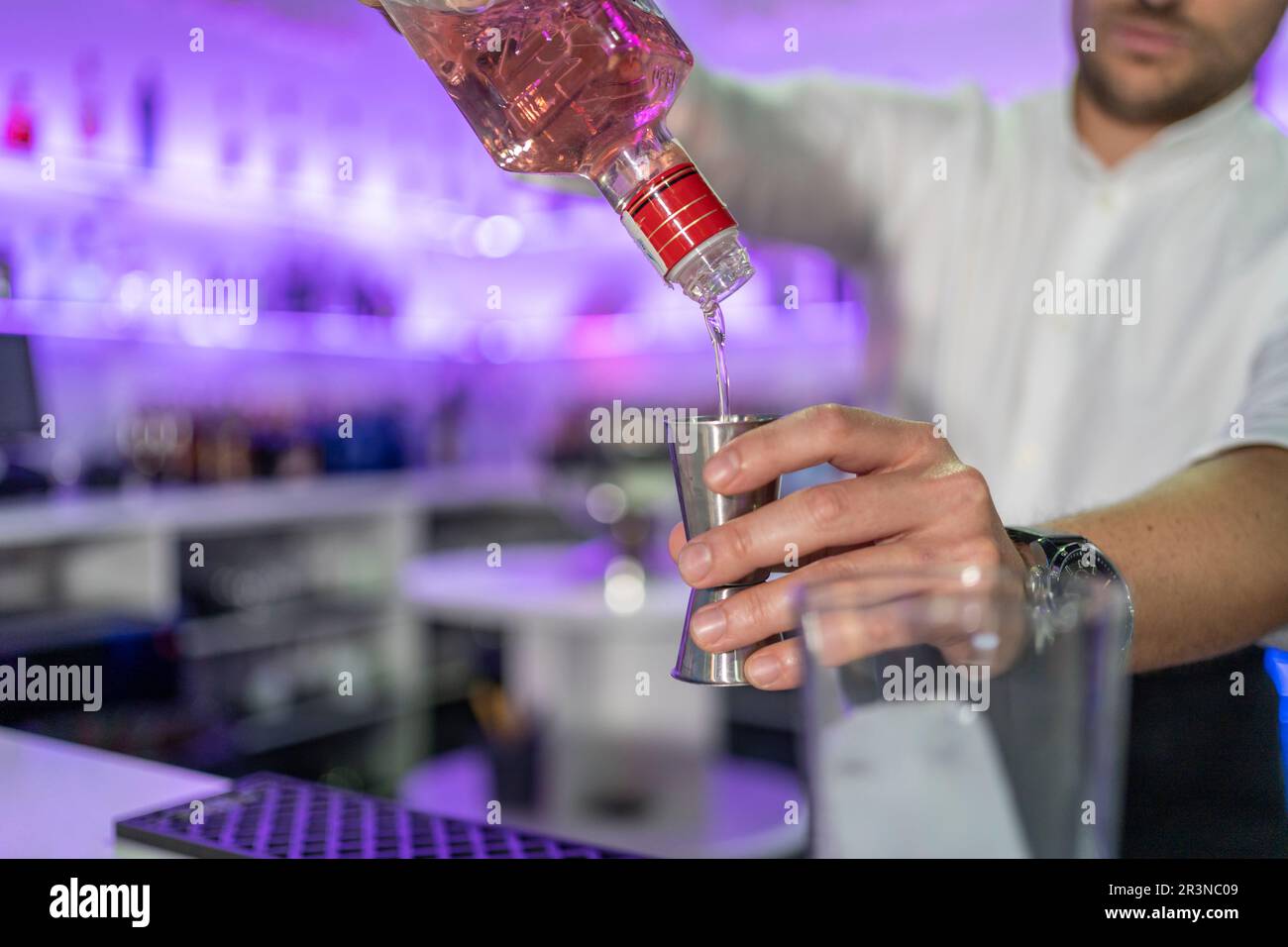 Unrecognizable male barkeeper pouring alcohol from bottle into jigger while standing and working ...