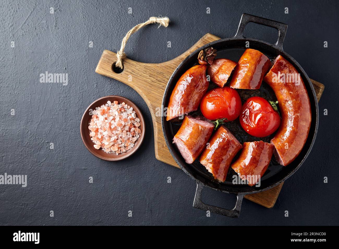 Portion cuts of fried pork sausage in a cast iron pan with tomatoes and ...