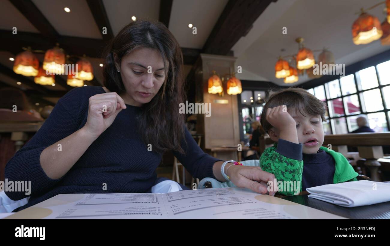 Mother and child sitting at restaurant table looking at menu. Mom ...