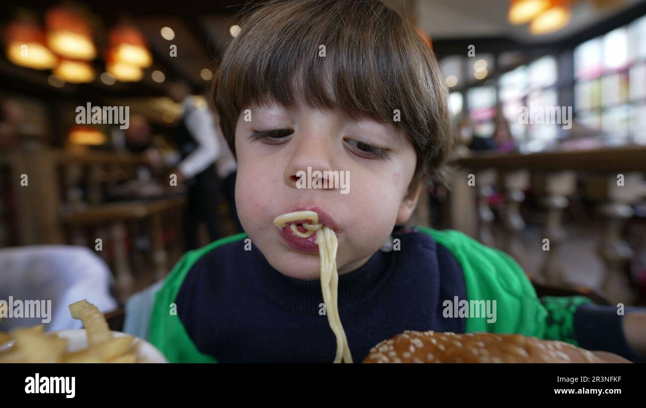 Child eating spaghetti pasta sitting at restaurant. Portrait closeup ...