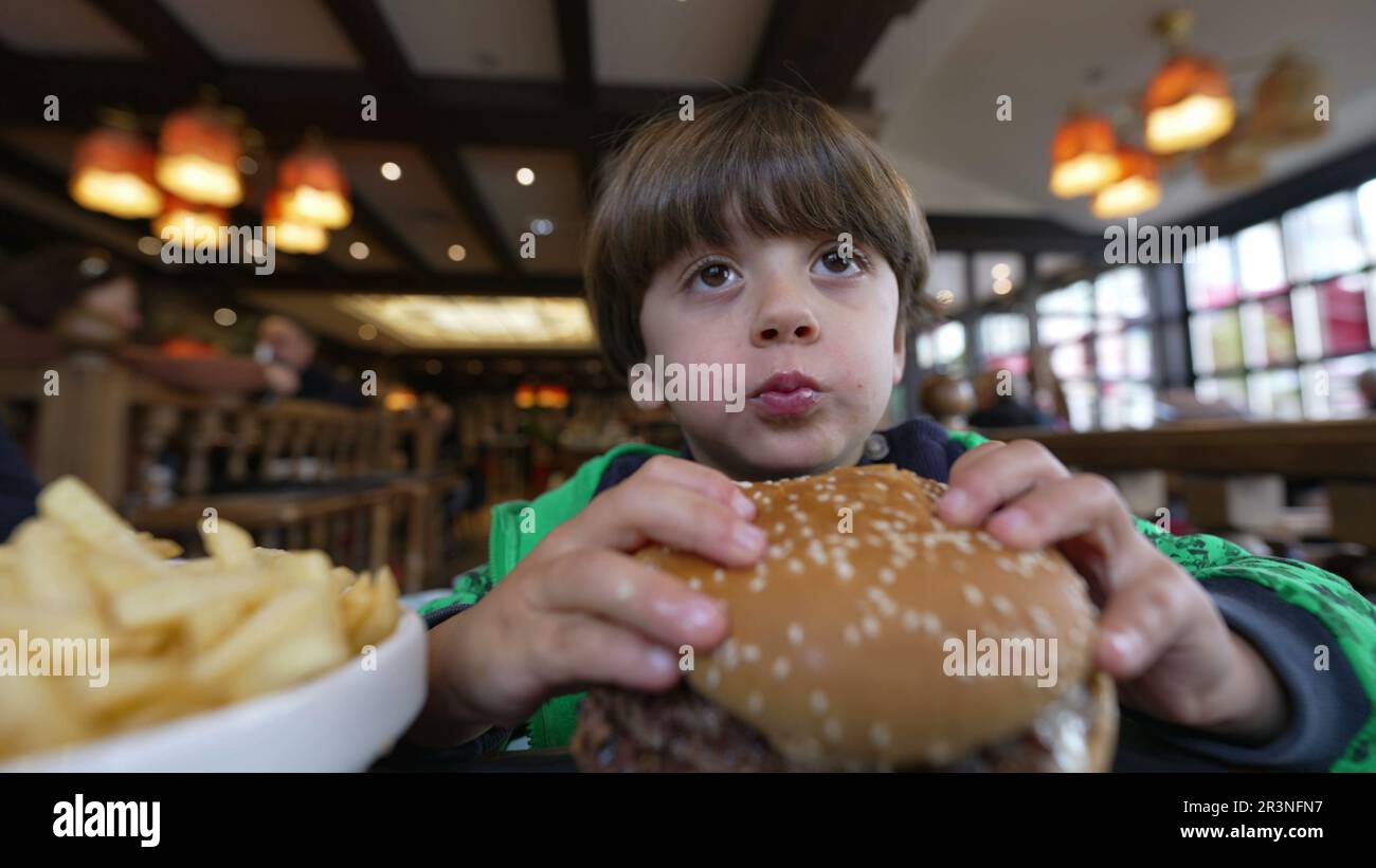 Child grabbing burger and eating. One little boy holding big hamburger ...