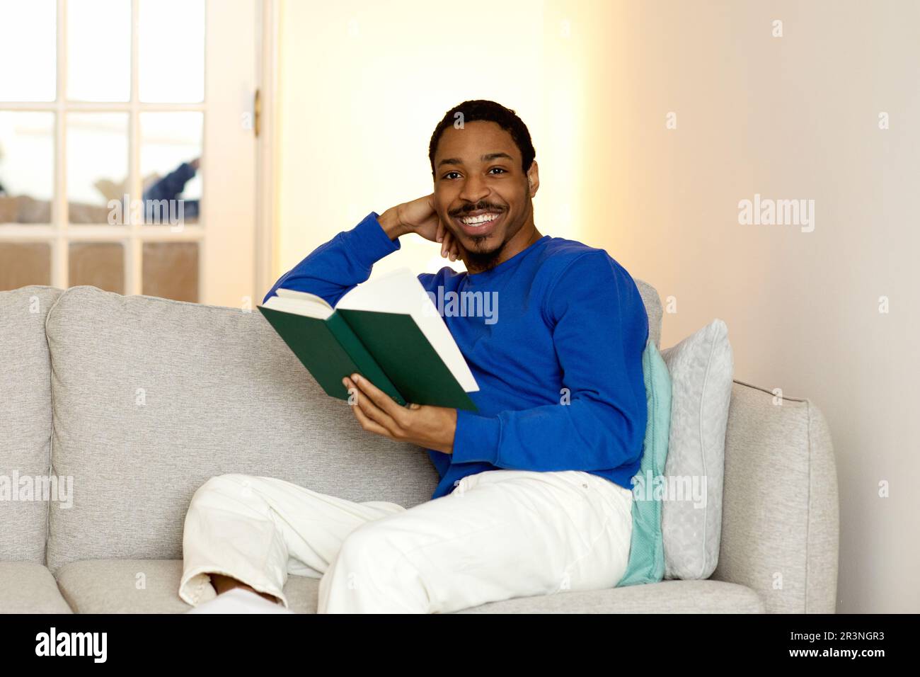 African Guy Reading Book Smiling To Camera Sitting At Home Stock Photo ...