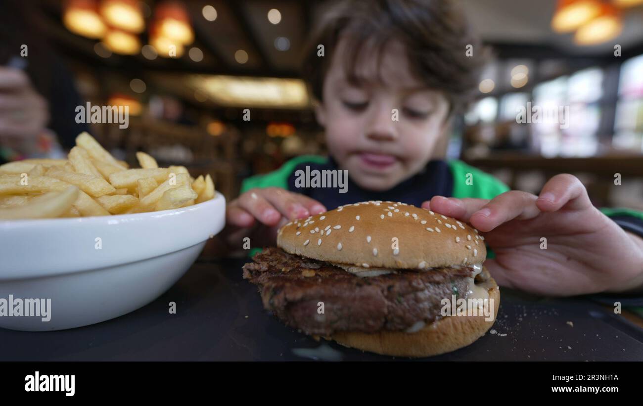 One small boy eating hamburger meal sitting at restaurant. Pensive ...