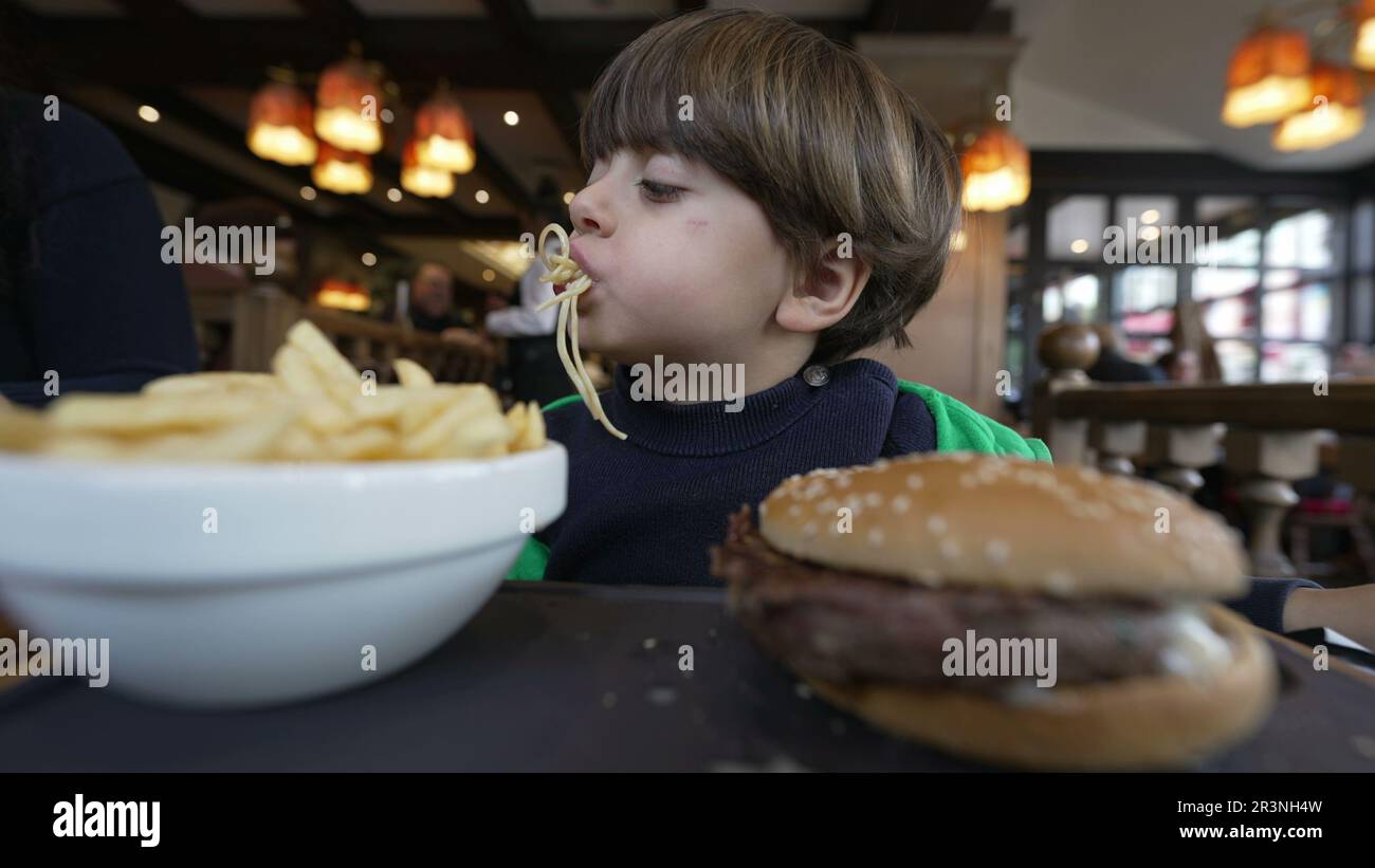 Mother feeding pasta to child sitting inside restaurant. Lifestyle mom ...