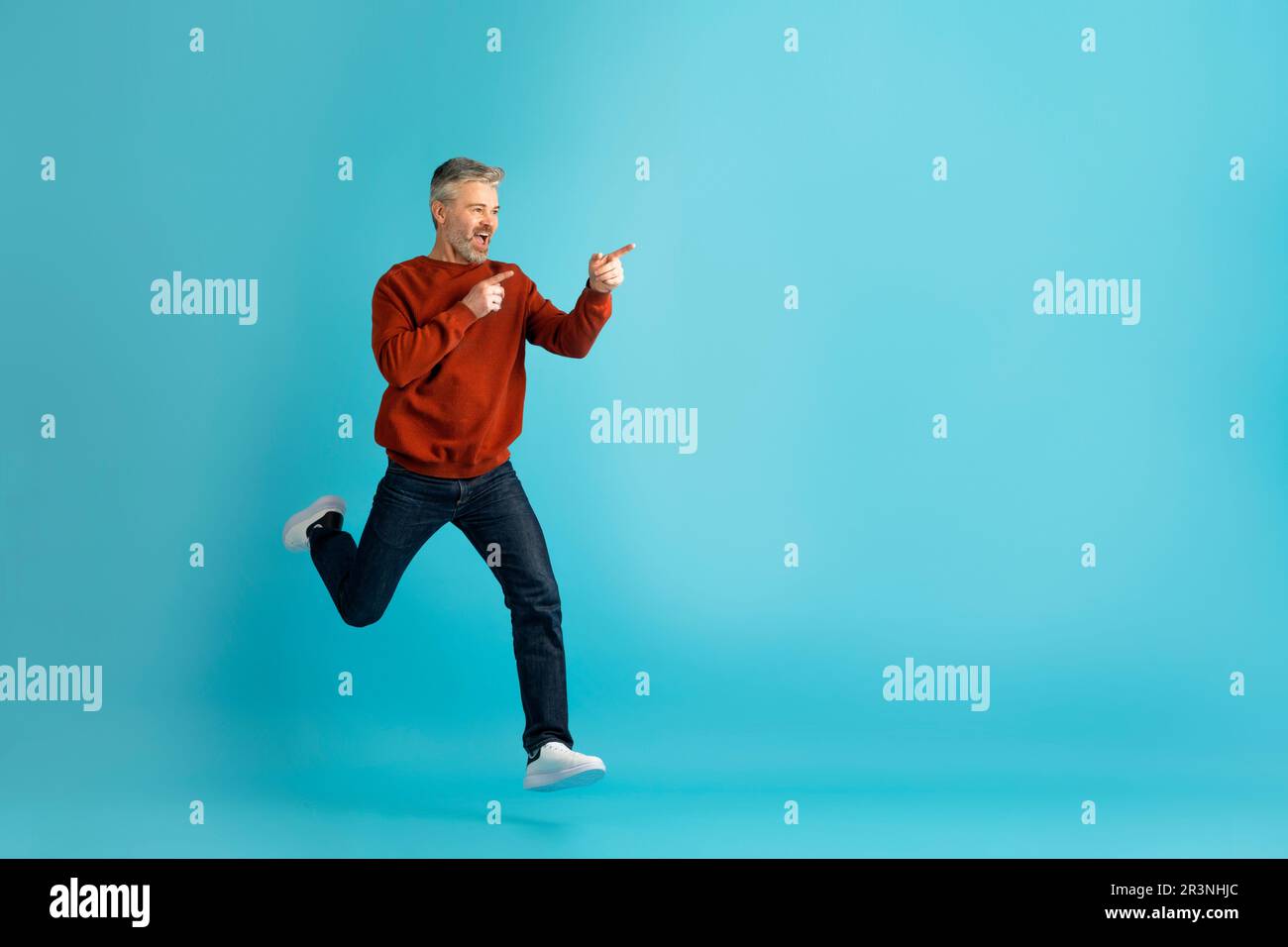 Excited middle aged man running towards copy space on blue Stock Photo ...