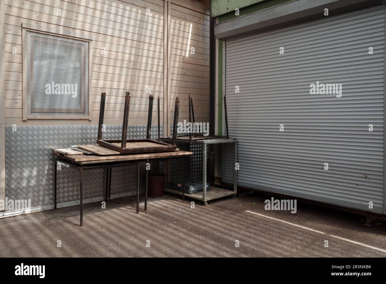 Exterior view in front of closed storefront, stack of stall tables, and ...