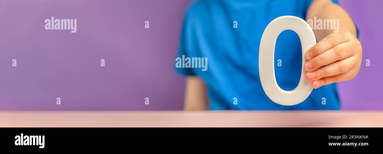 Number 0 in hand. Hand holding white number zero over green grass and ...