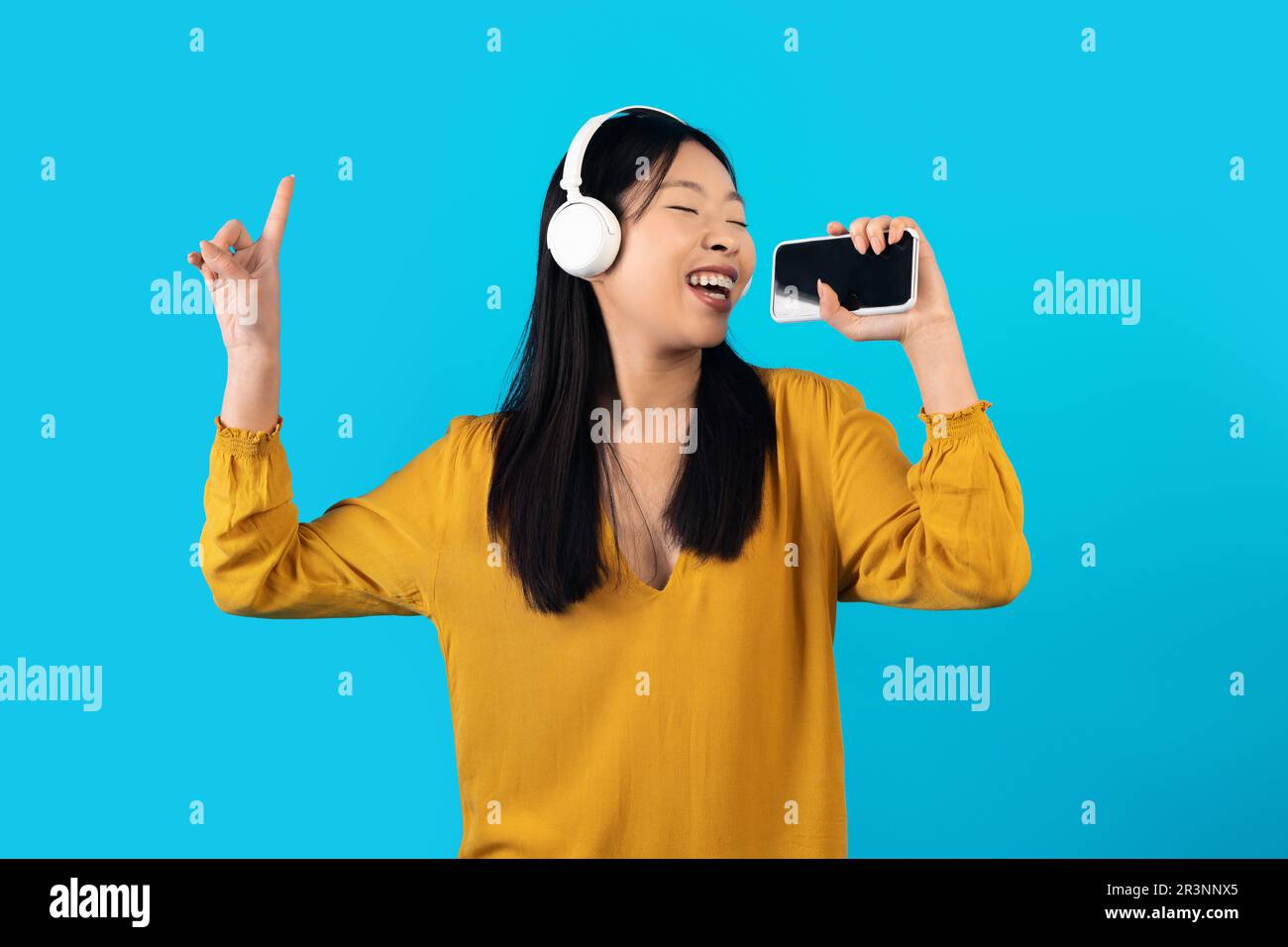 Joyful chinese woman singing karaoke on blue Stock Photo - Alamy