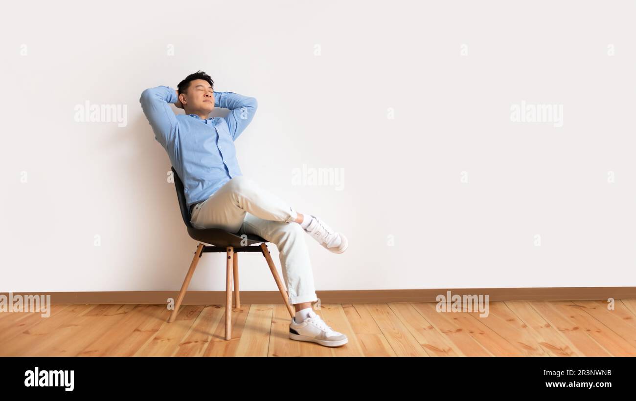 Calm asian mature man relaxing sitting on chair, leaning back holding ...