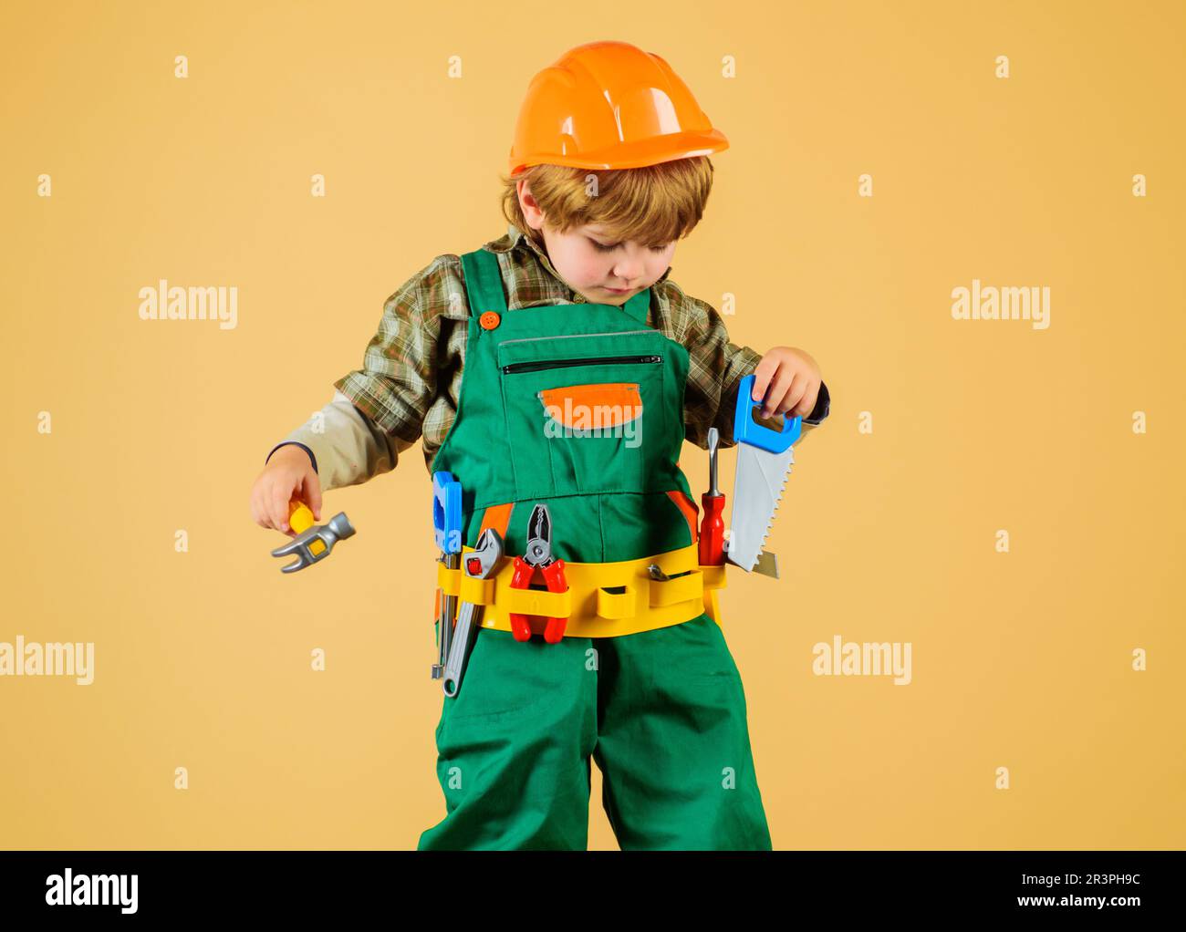 Little child boy in safety helmet and toolbelt with saw and hammer ...