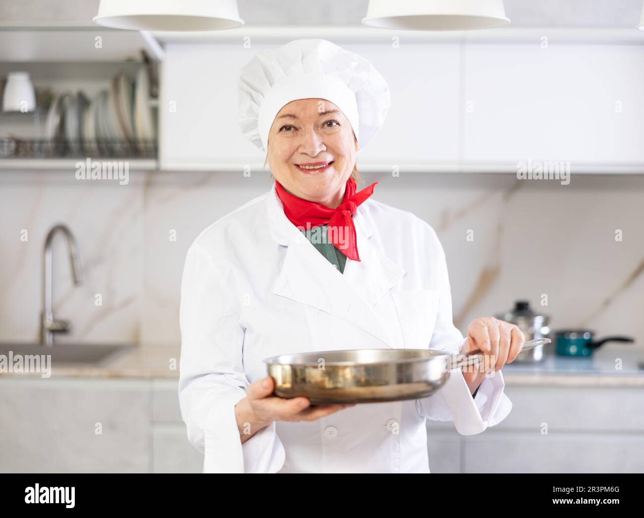 Confident mature woman in cook outfit showing around hew kitchen Stock ...