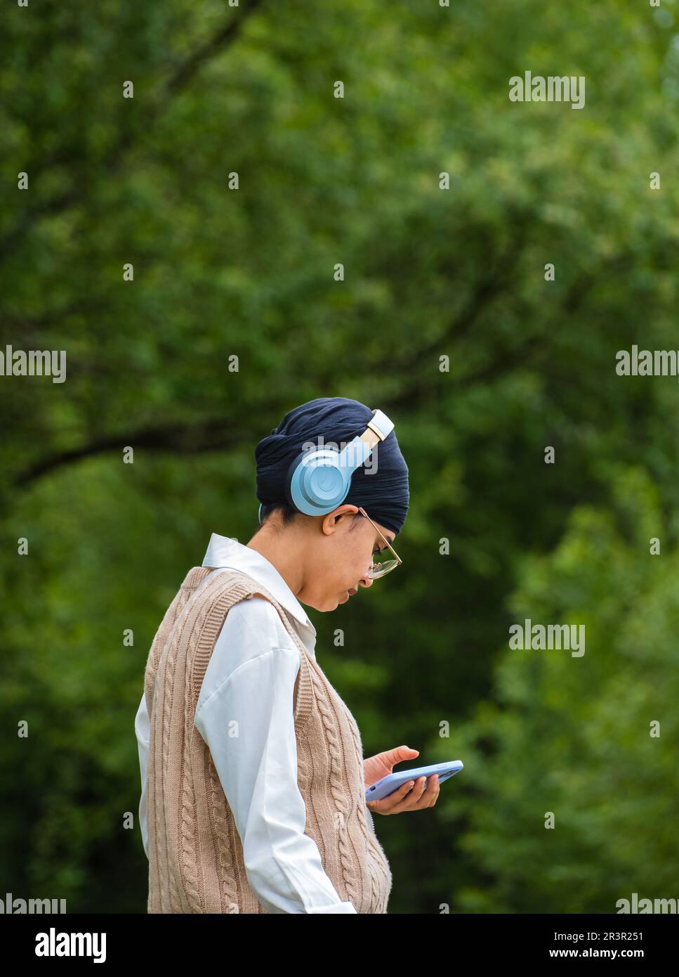 Young girl using phone to listen music on her headphones in the park ...