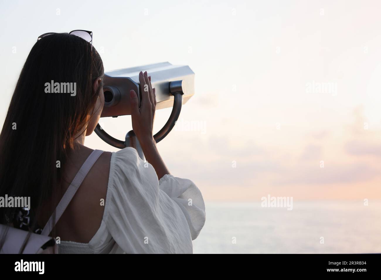 Young woman looking through tourist viewing machine at observation deck ...