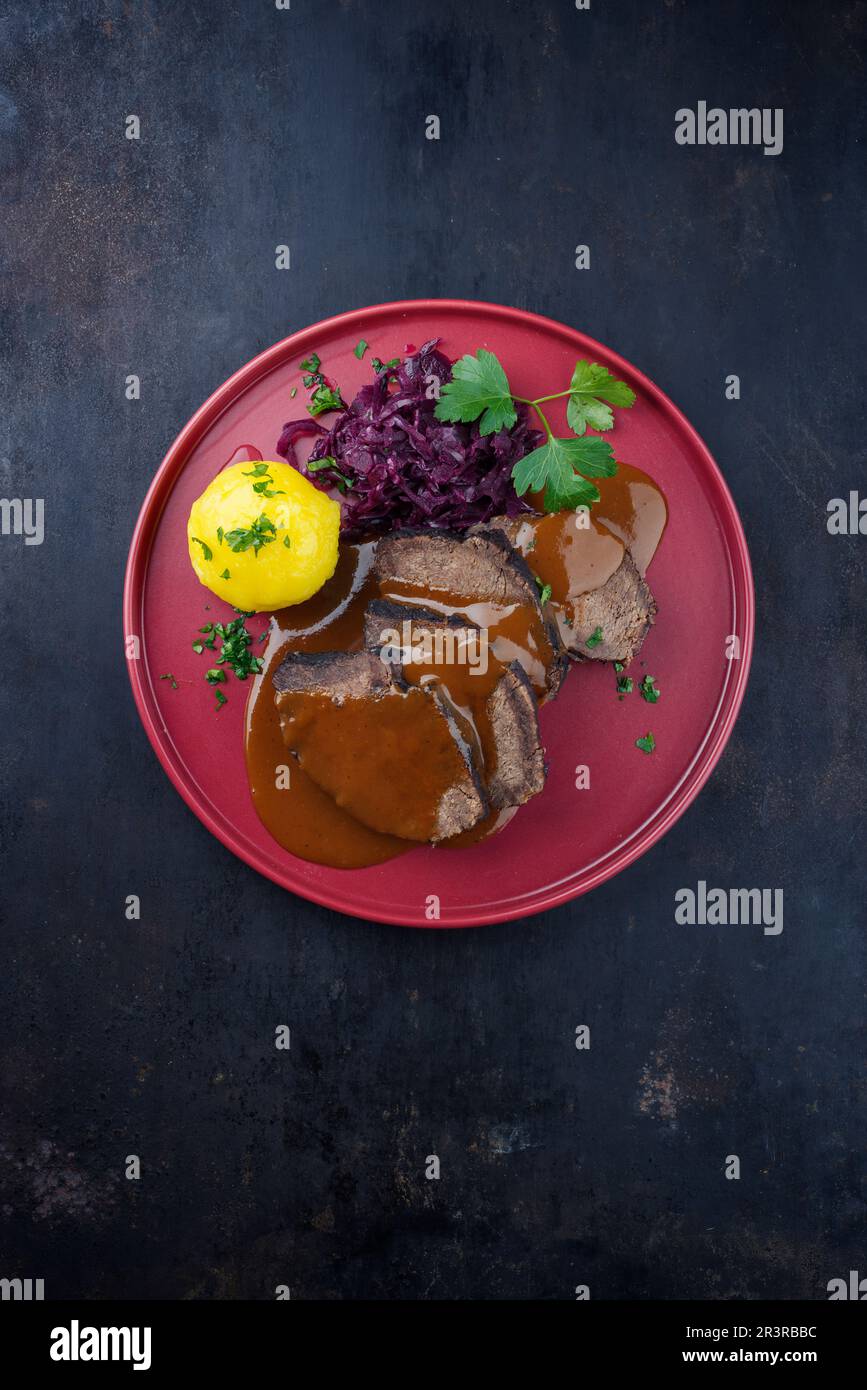 Traditional braised marinated German Sauerbraten from beef with blue kraut and potato dumplings ...