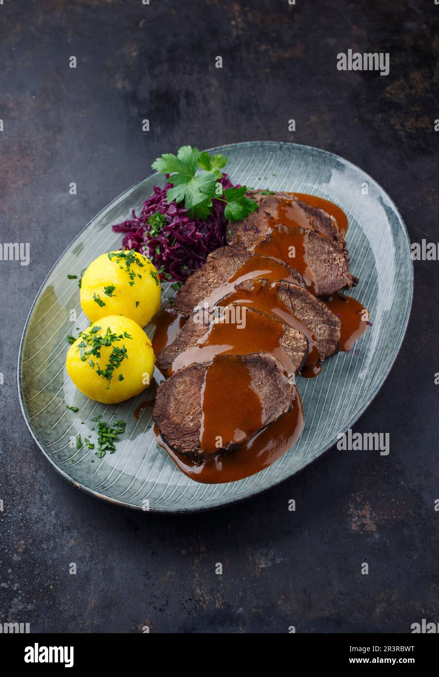 Traditional braised marinated German Sauerbraten from beef with blue kraut and potato dumplings ...