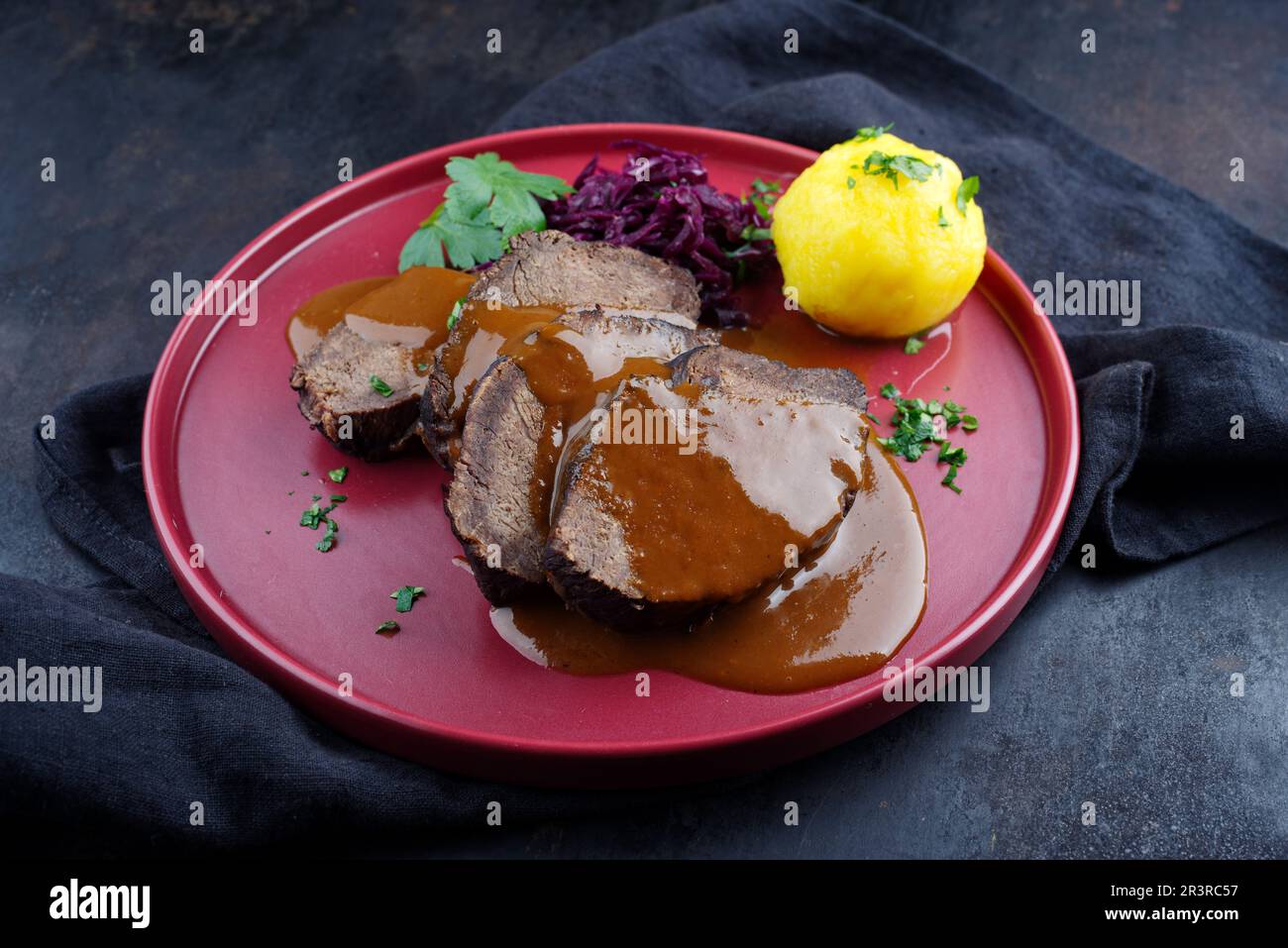Traditional braised marinated German Sauerbraten from beef with blue kraut and potato dumplings ...