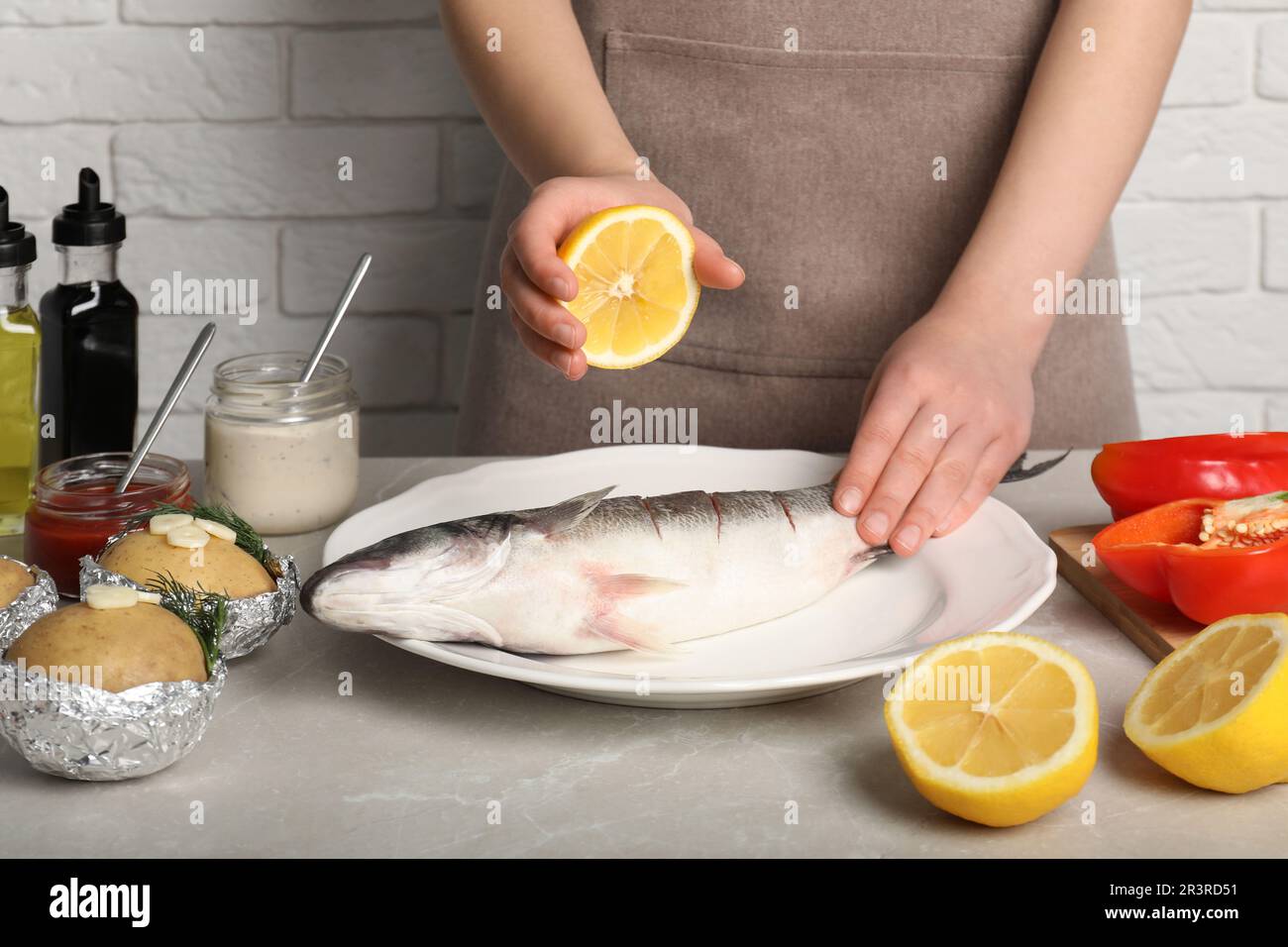 Woman squeezing lemon juice on fresh sea bass fish at light gray marble ...