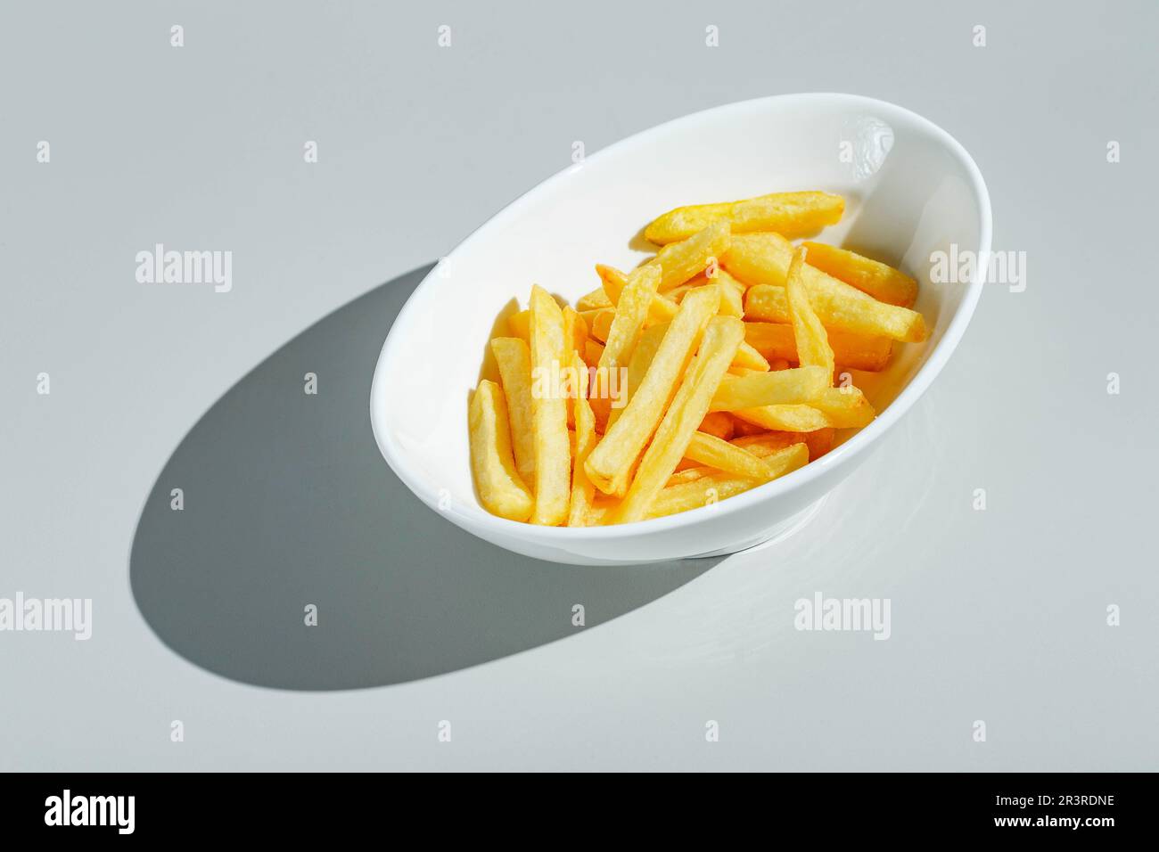 French fries in white bowl on light background. Hard light, deep shadow ...