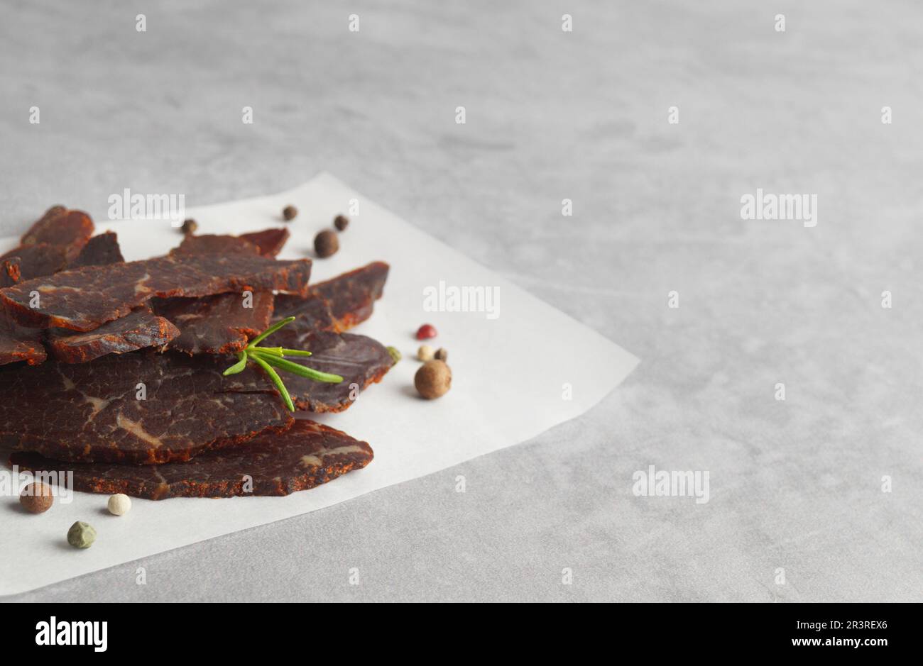 Pieces of delicious beef jerky and spices on light grey table. Space ...