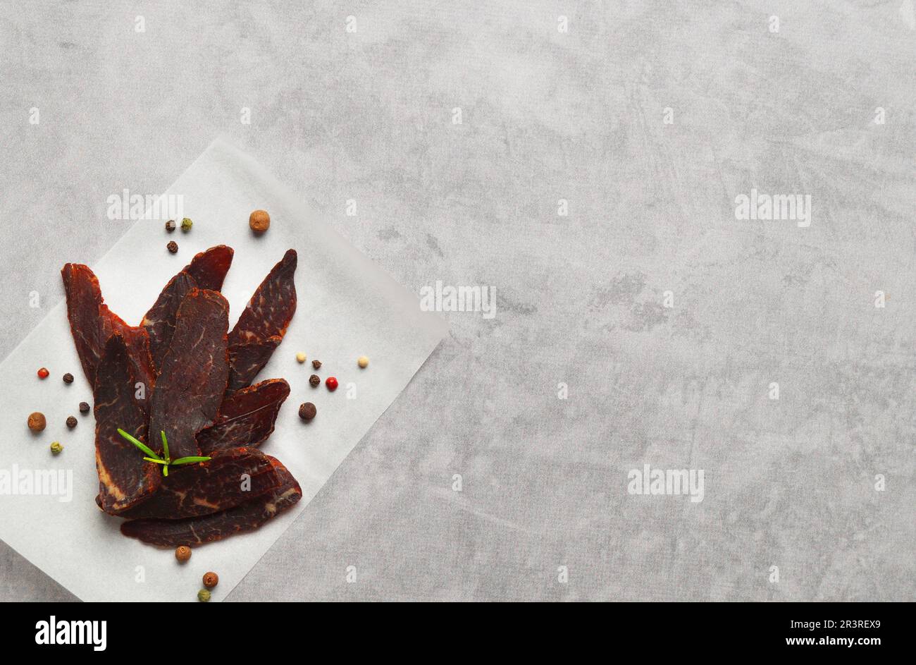 Pieces of delicious beef jerky and spices on light grey table, top view ...