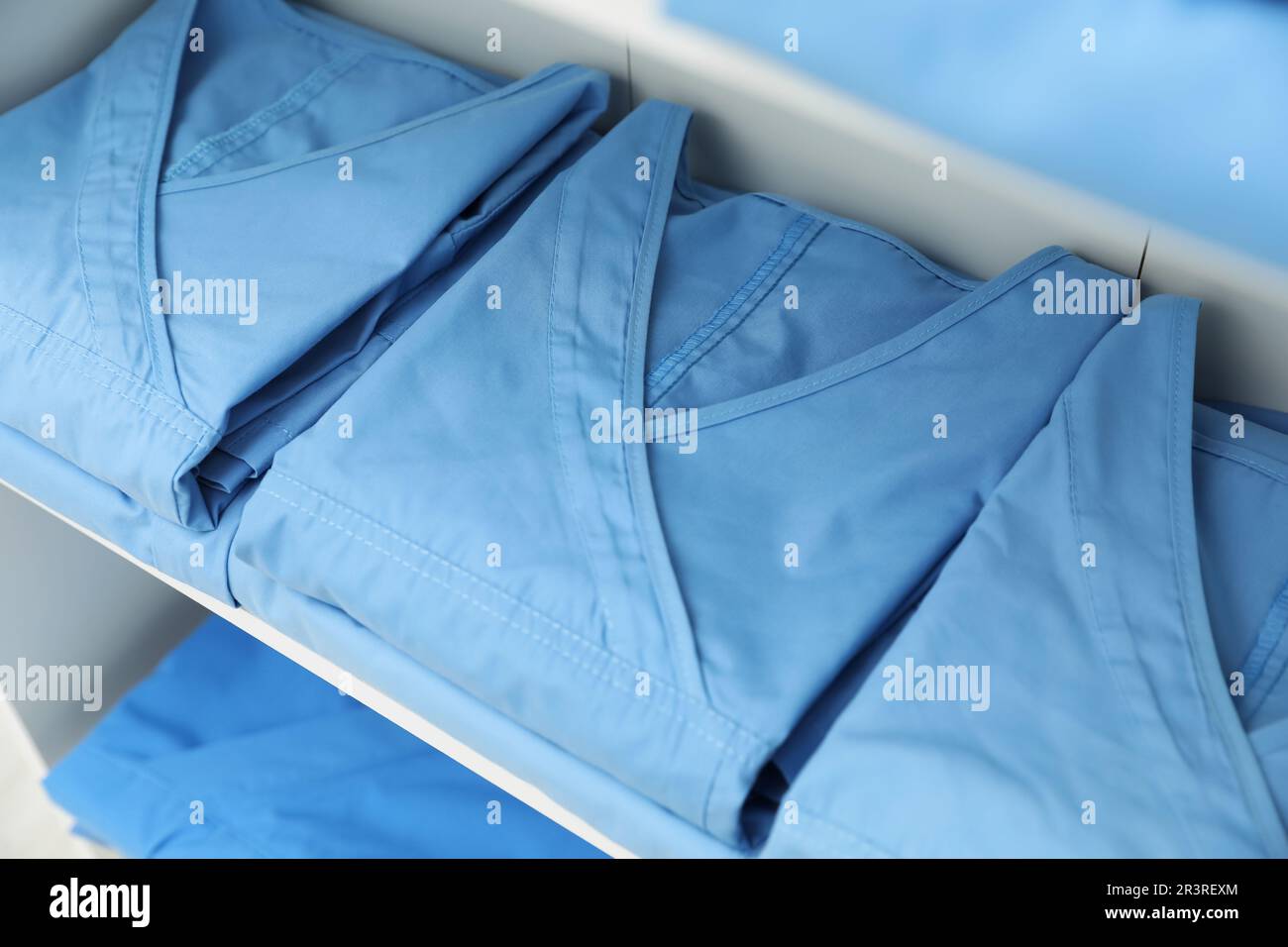 Light blue medical uniforms on white rack, closeup Stock Photo - Alamy