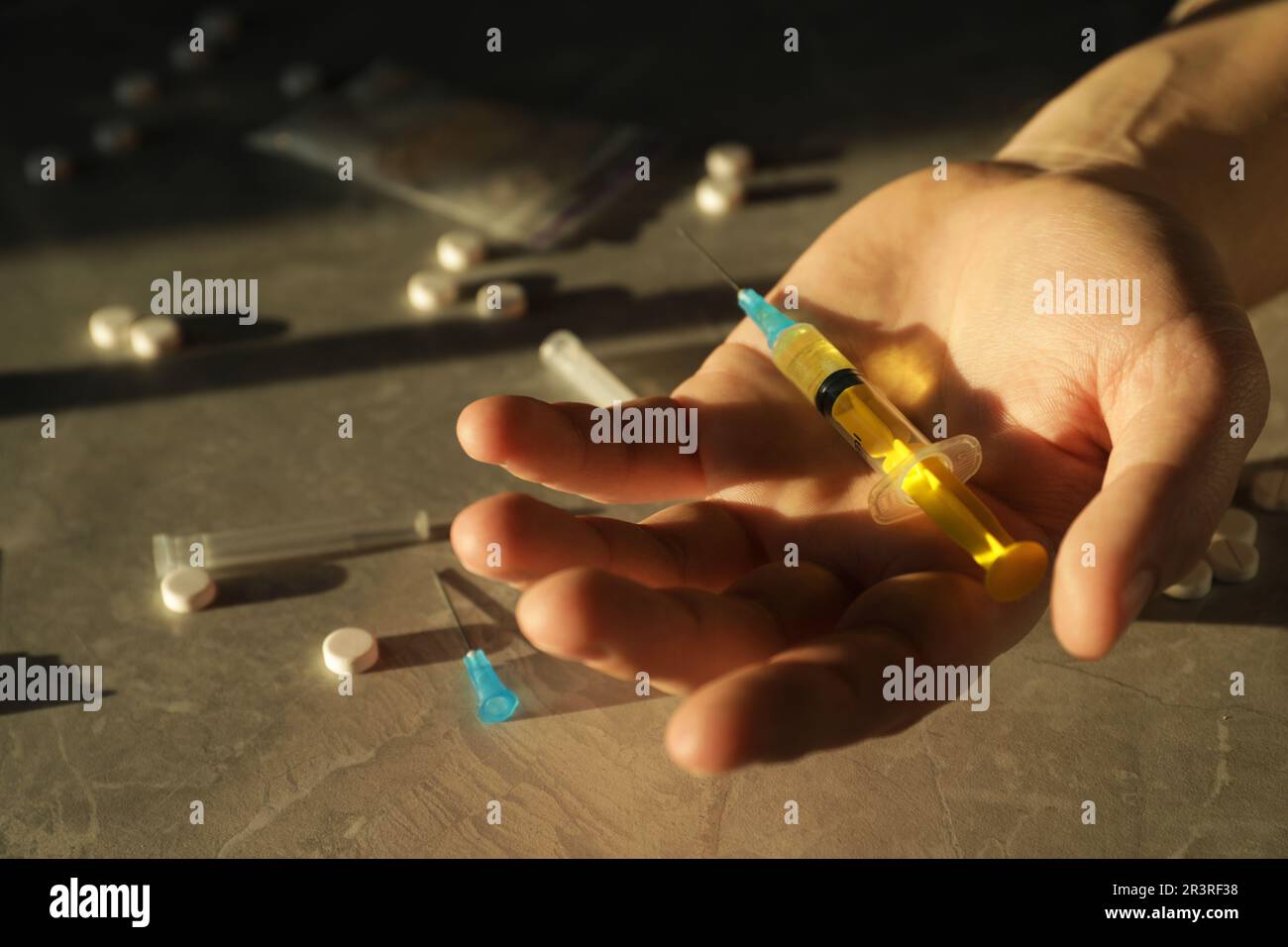 Addicted man holding syringe near drugs at grey textured table ...