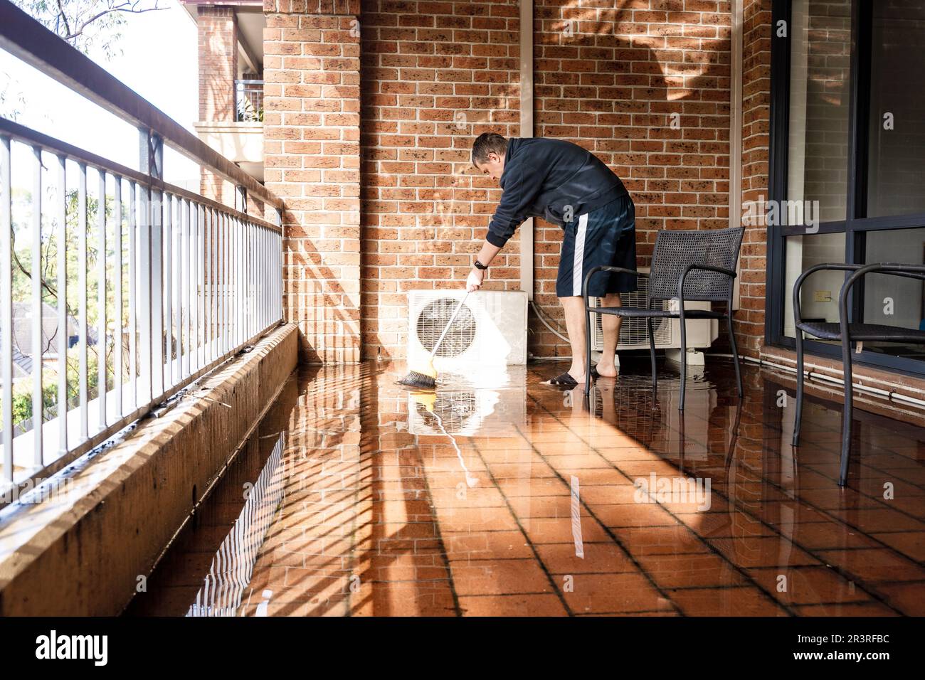 A man cleaning flooded balcony balcony after heavy rain Stock Photo - Alamy