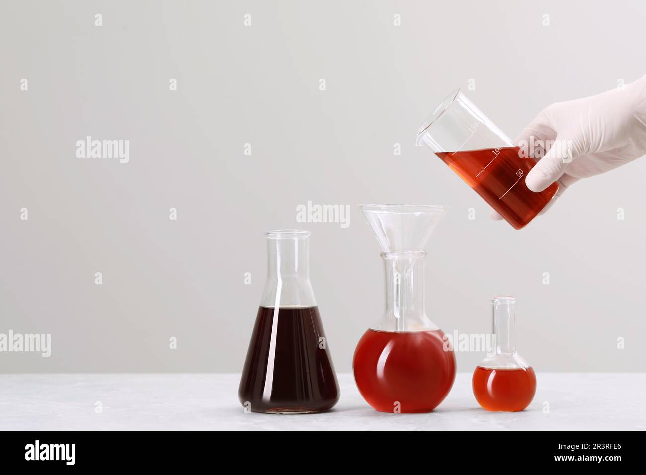 Scientist pouring liquid from beaker into round bottom flask on white ...