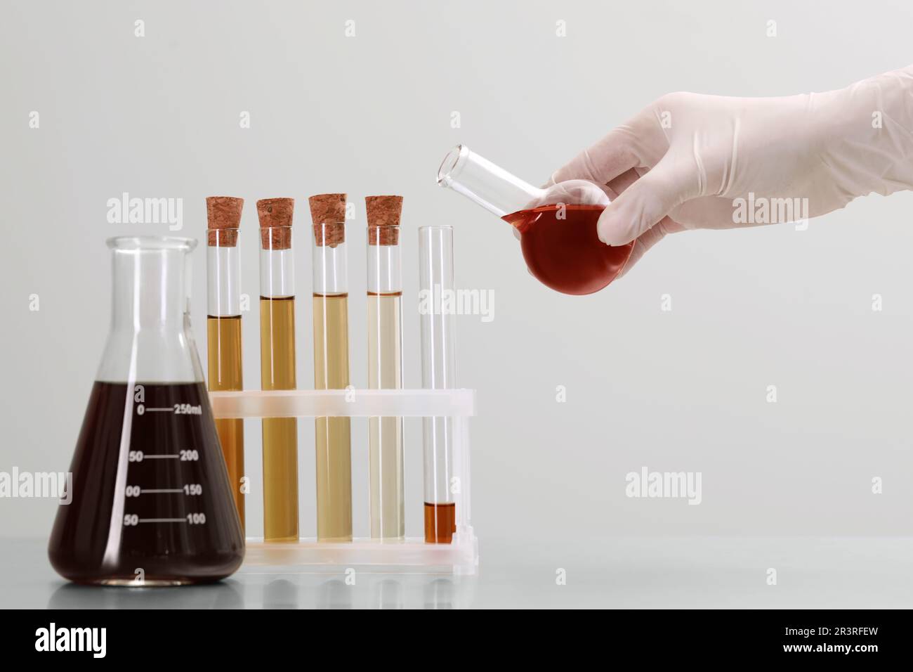 Scientist pouring brown liquid from round bottom flask into test tube ...