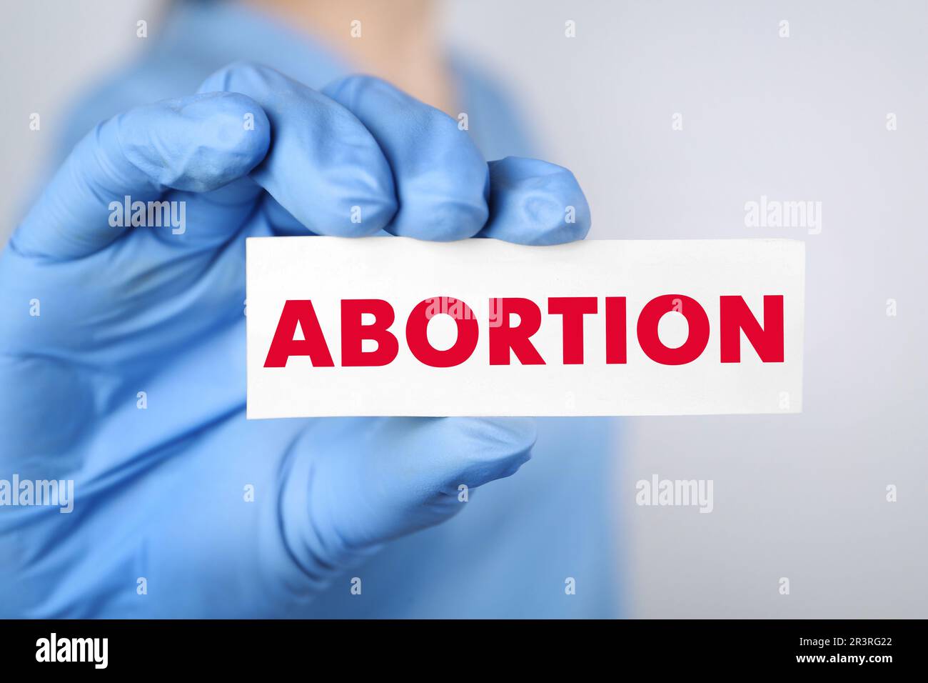 Doctor holding paper card with word Abortion on light grey background ...