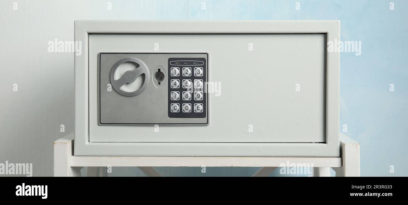 Closed steel safe on white table against light blue background, banner ...