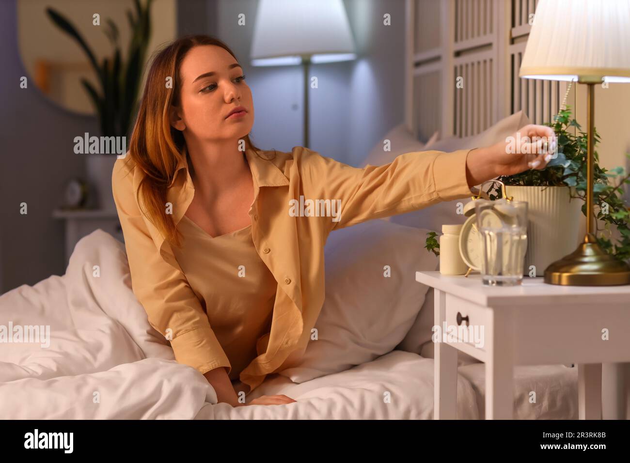 Young woman turning off lamp before sleep in bedroom Stock Photo - Alamy