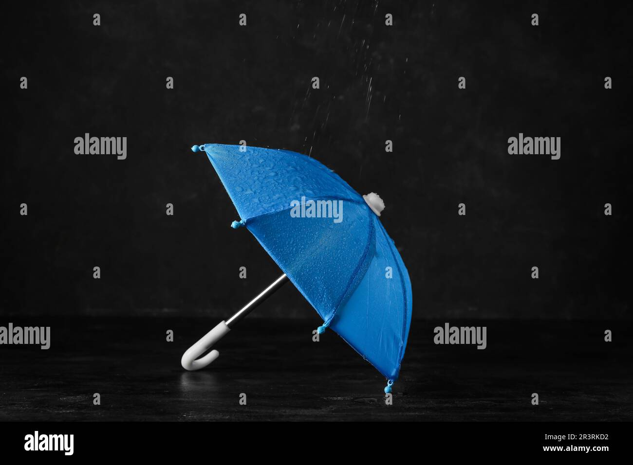 Mini blue umbrella with water drops on black background Stock Photo - Alamy