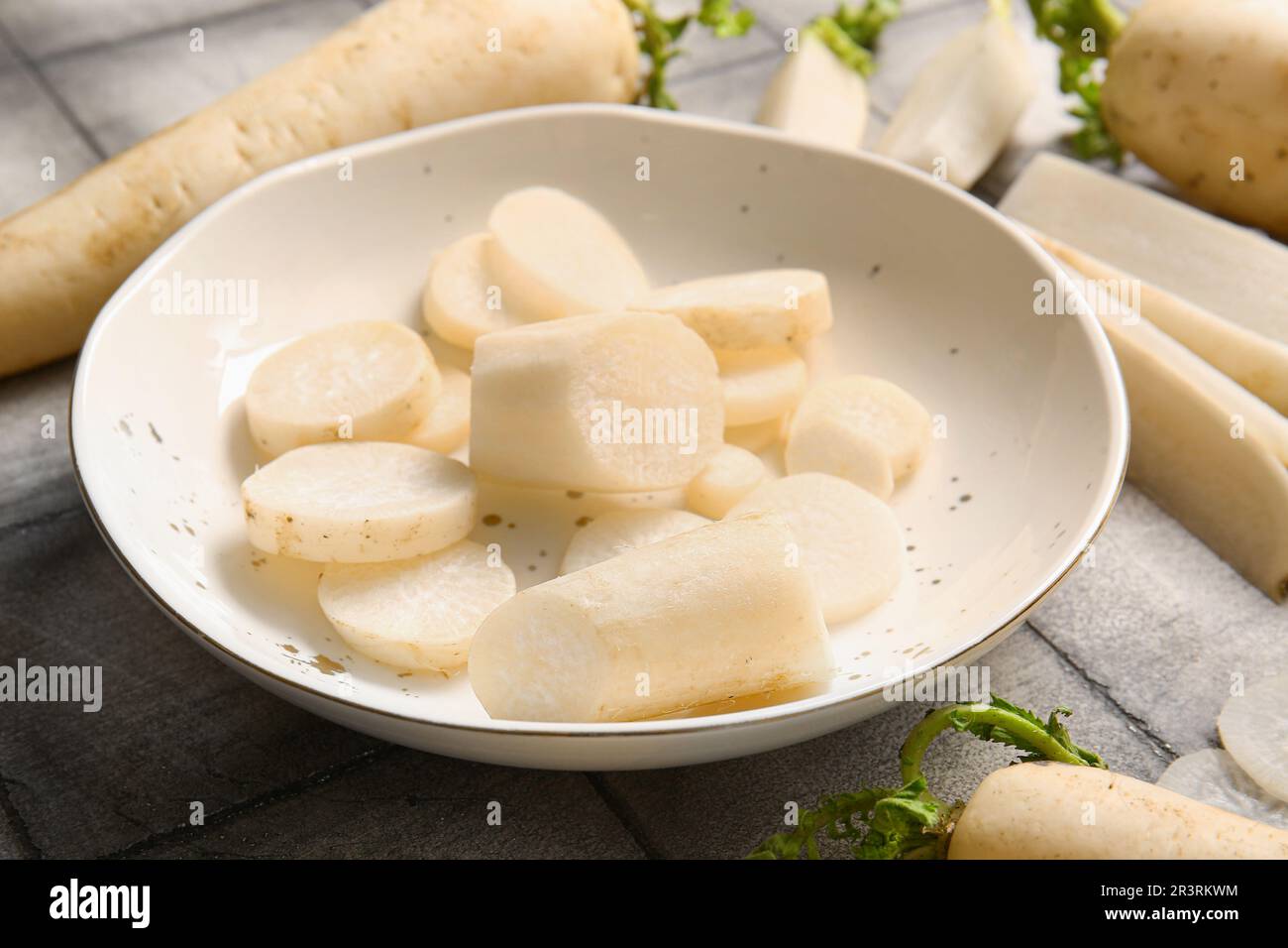 Bowl with slices of fresh daikon radish on grey tile background Stock ...