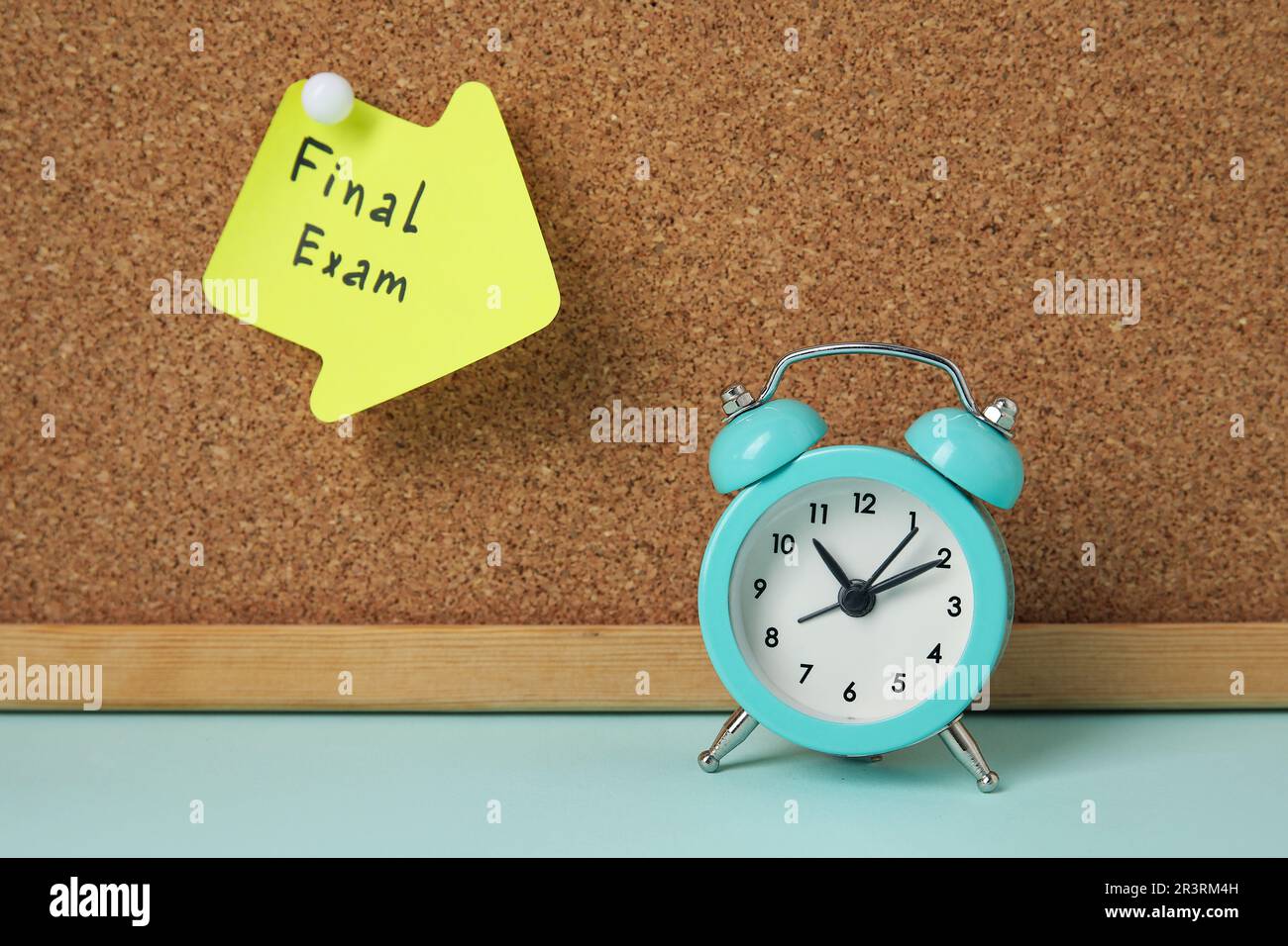Sticky note with text FINAL EXAM hanging at cork board and alarm clock ...