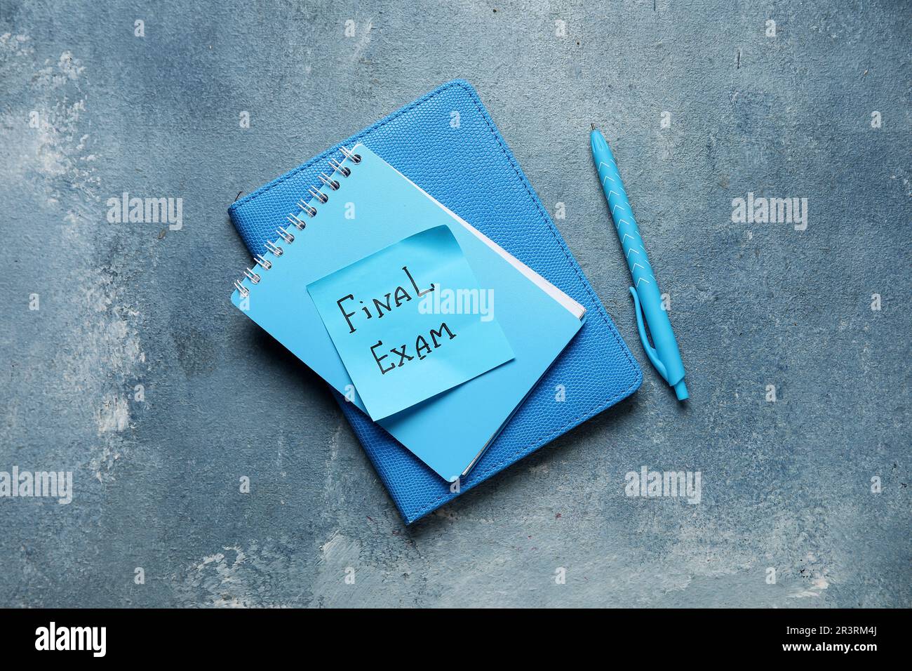 Sticky note with text FINAL EXAM, notebooks and pen on grunge blue ...
