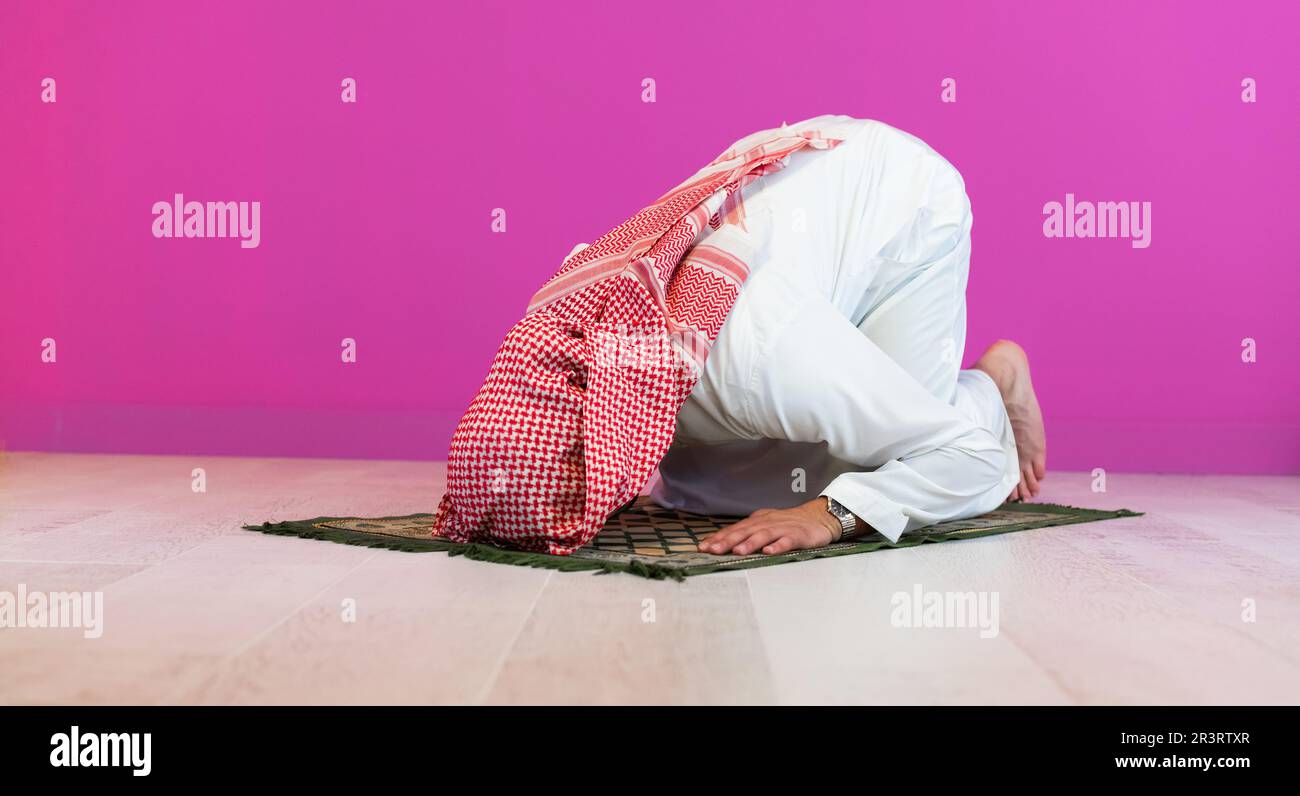 Young arabian muslim man in traditional clothes praying on the carpet ...