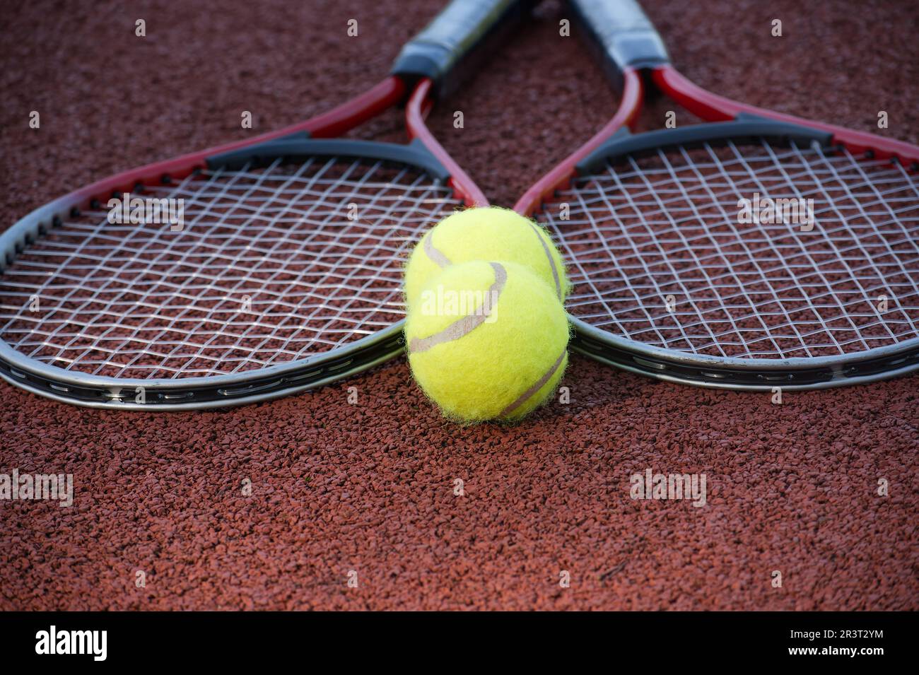 Two yellow tennis balls and two racquets on hard tennis court surface ...