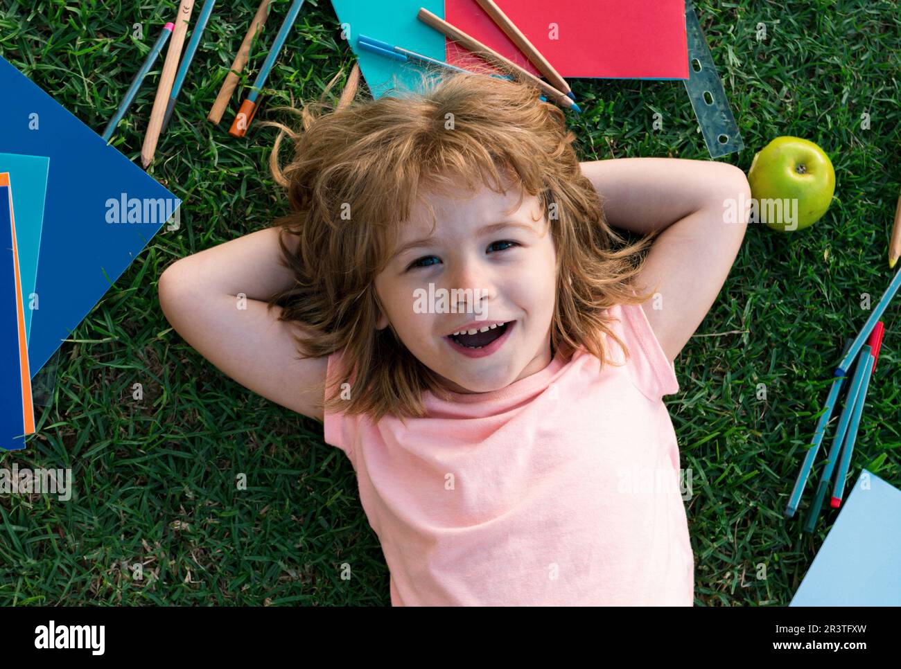 Fanny smiling face of cute smart school boy, lie on grass. Happy pupil ...