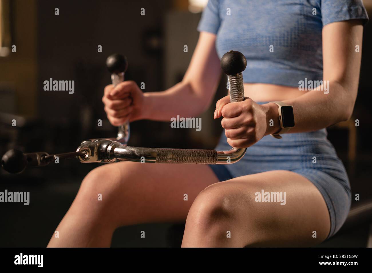 Strong woman sitting while rowing at the cable machine for back muscles ...