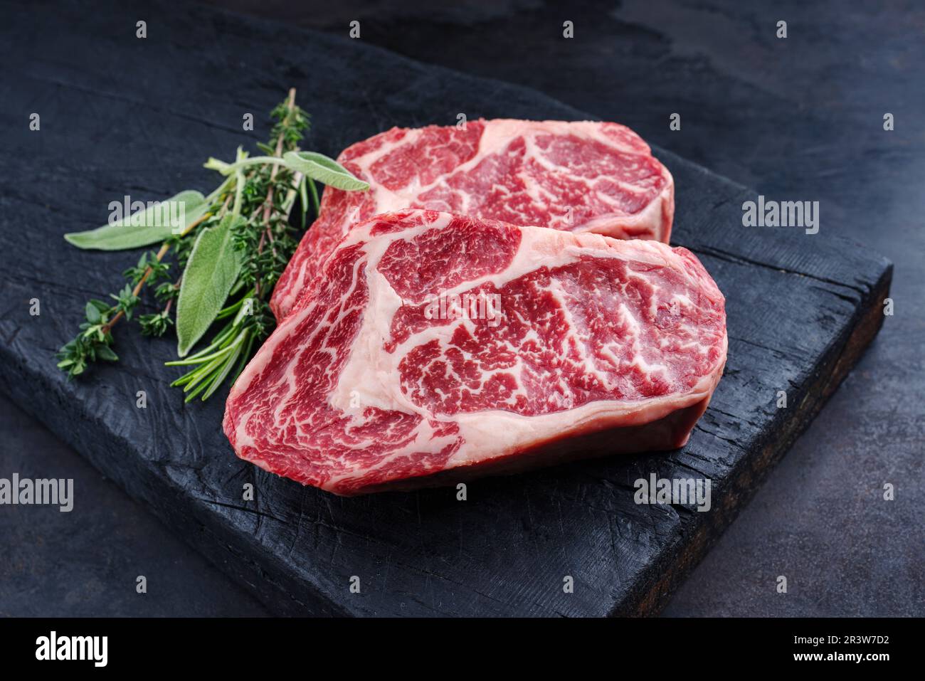Two raw dry aged wagyu rib-eye beef steaks with herbs offered as close ...