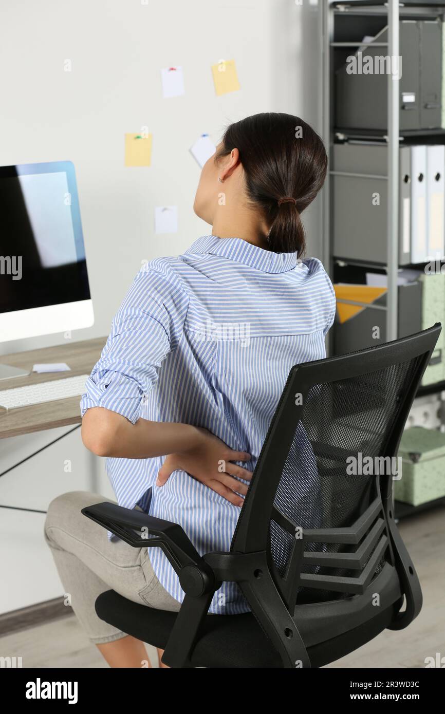 Young woman suffering from back pain while sitting in office. Symptom ...
